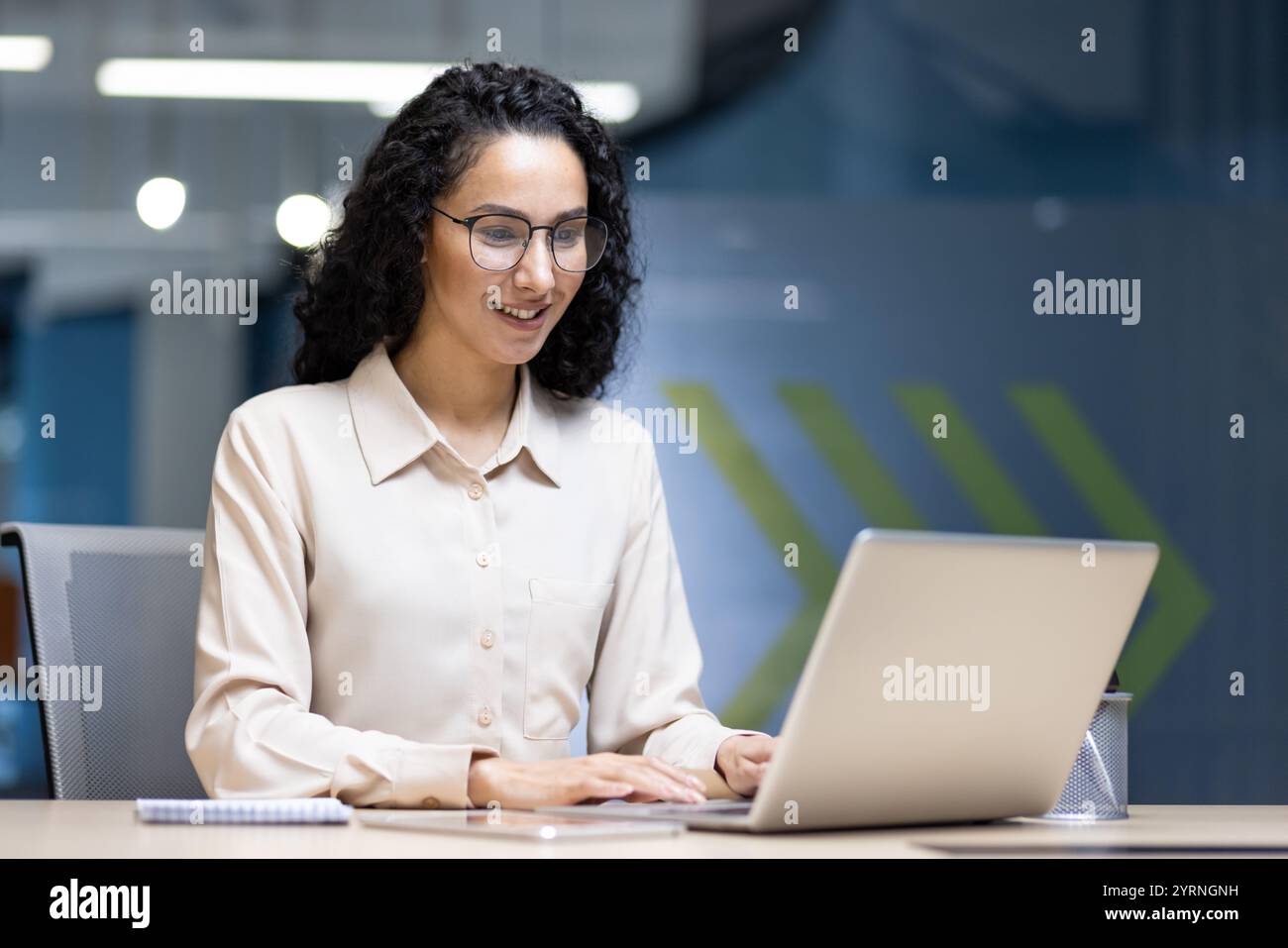 A confident businesswoman is typing on her laptop in a modern office ...