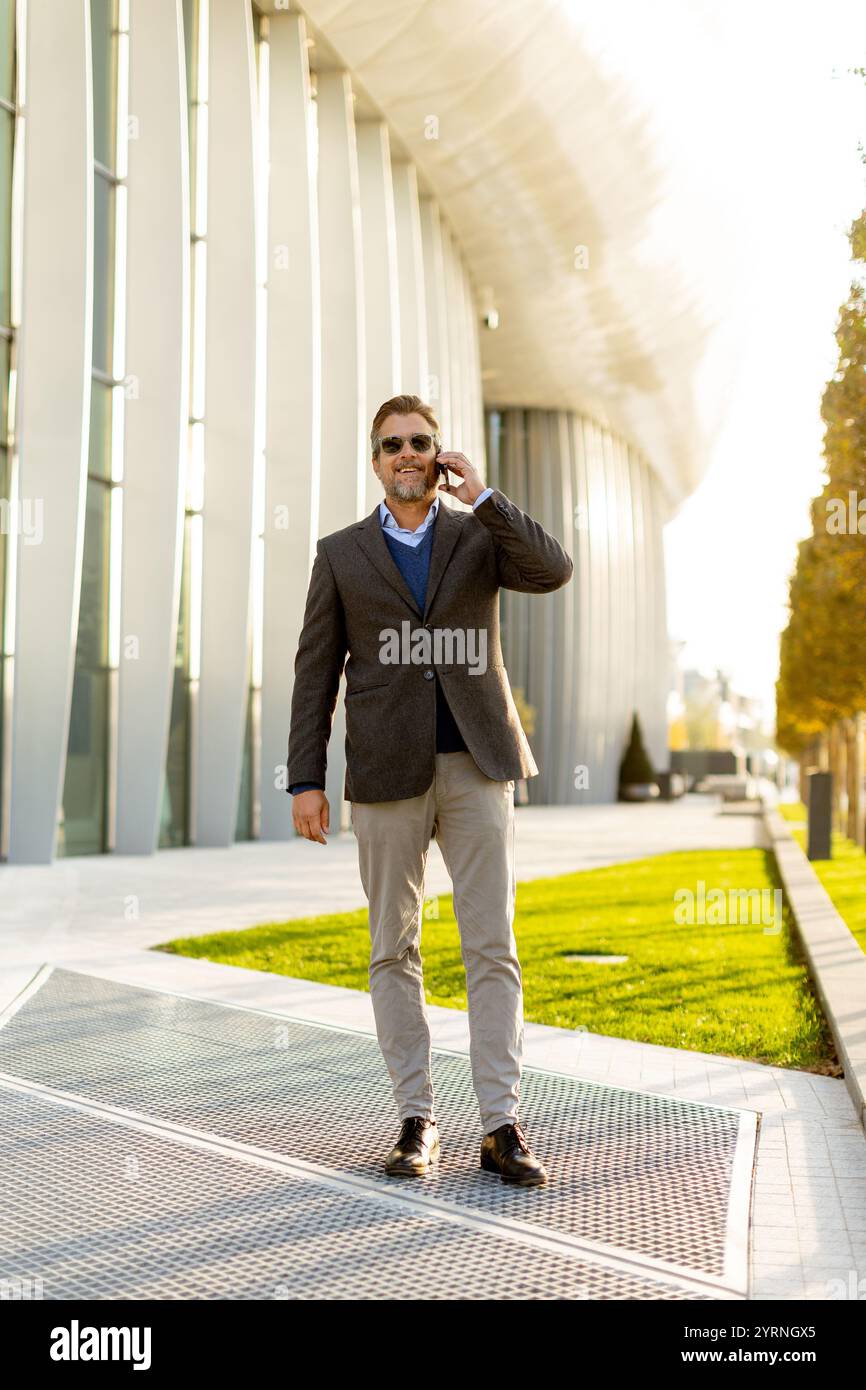 A well-dressed man strolls along a sleek pathway, chatting on his phone ...