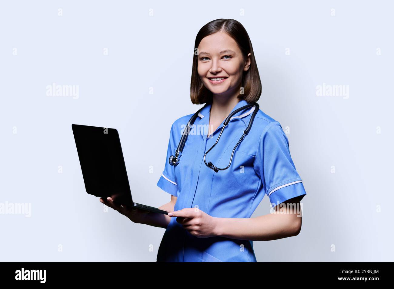 Female nurse with laptop, looking at camera on white studio background ...