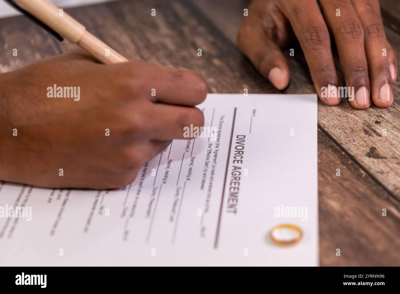 A person signs divorce papers, with a wedding ring discarded on the ...
