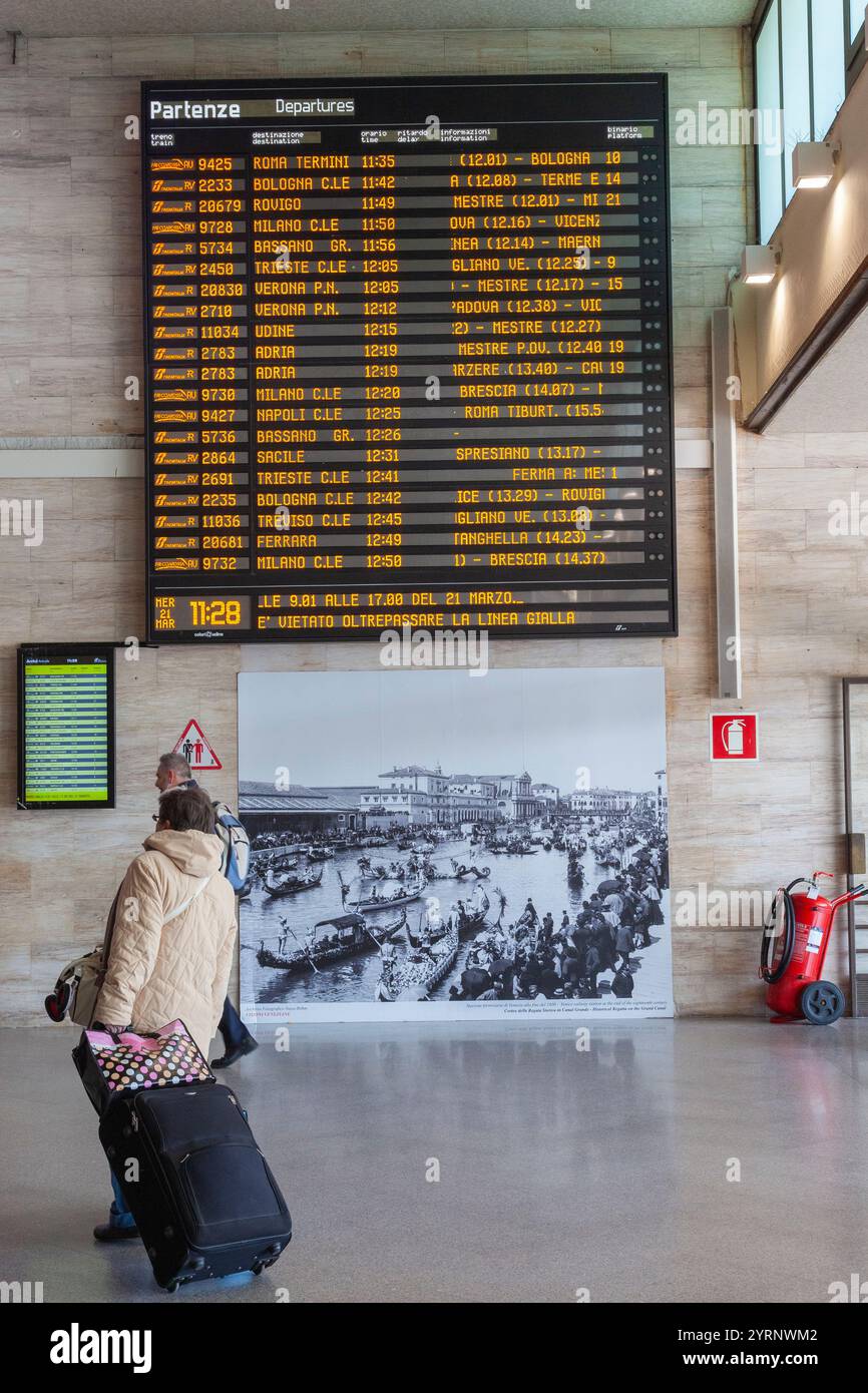 Tourist with luggage passing the departures board at Santa Lucia ...
