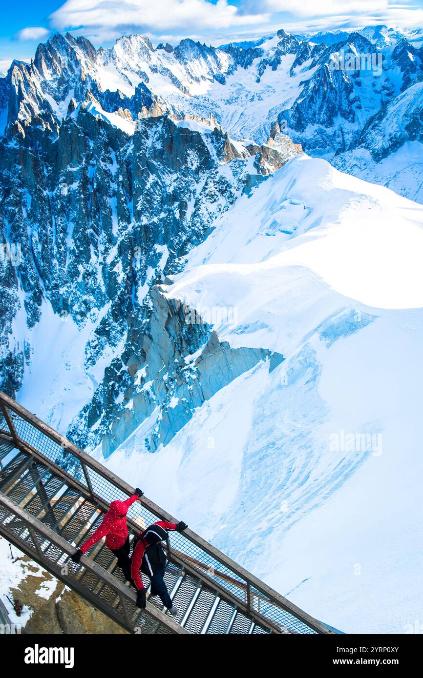 Two tourists in jackets walk on a metal walkway high above Chamonix ...