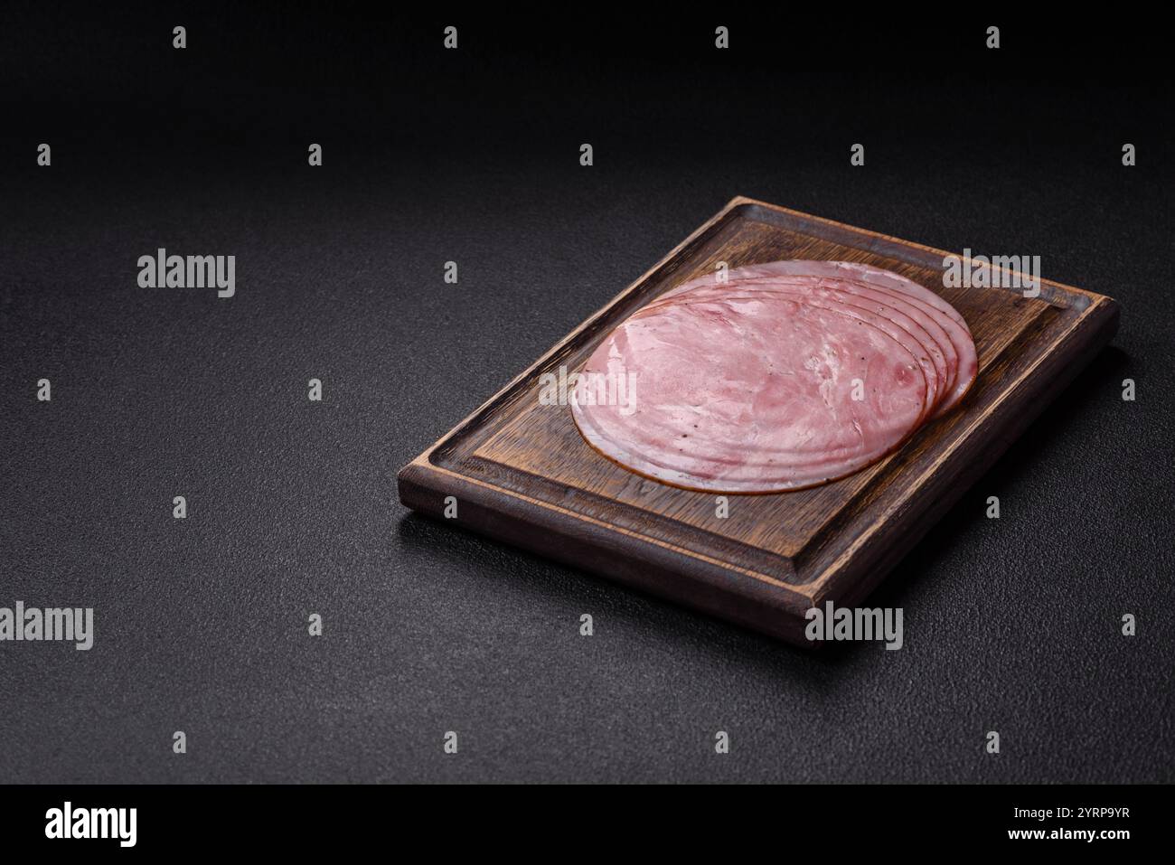 Smoked ham with salt, spices and herbs cut into round slices on a dark ...