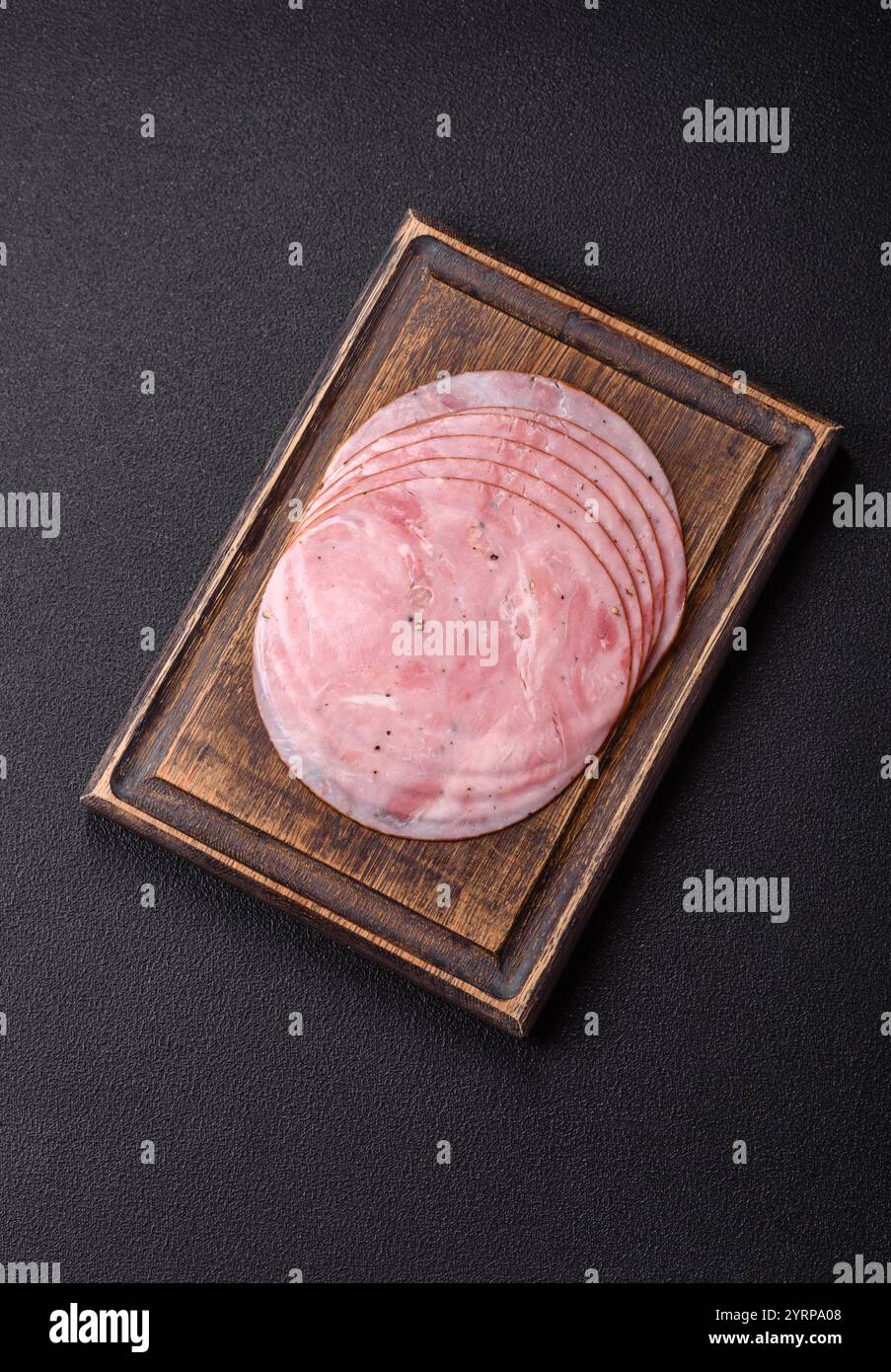 Smoked ham with salt, spices and herbs cut into round slices on a dark ...
