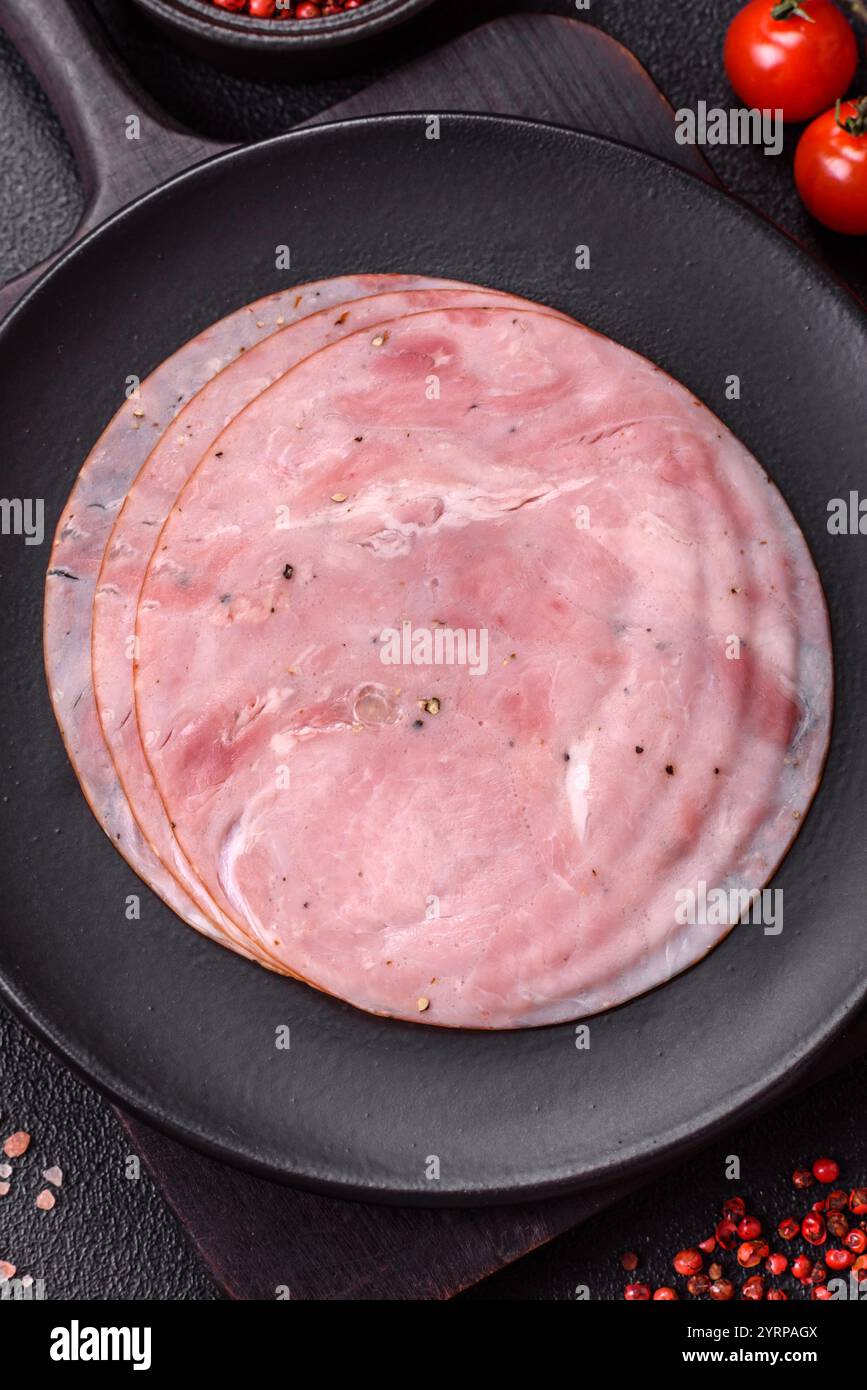Smoked ham with salt, spices and herbs cut into round slices on a dark ...