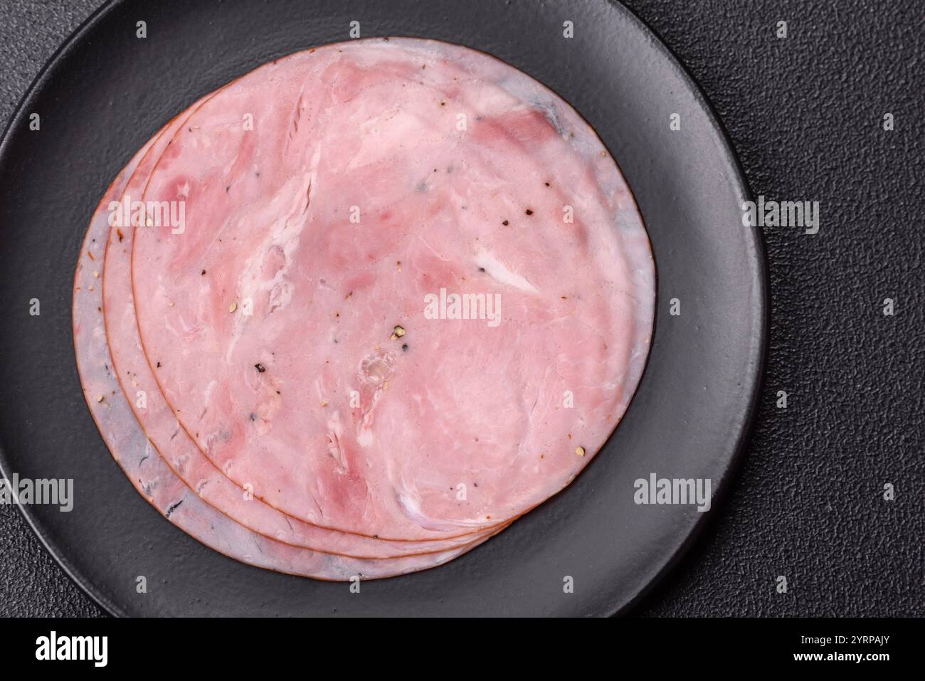 Smoked ham with salt, spices and herbs cut into round slices on a dark ...