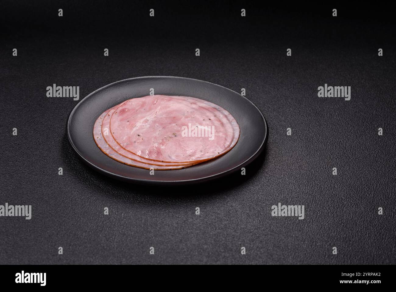 Smoked ham with salt, spices and herbs cut into round slices on a dark ...