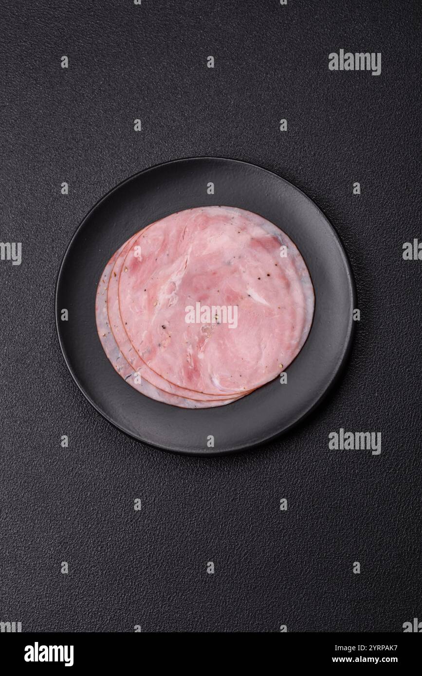 Smoked ham with salt, spices and herbs cut into round slices on a dark ...