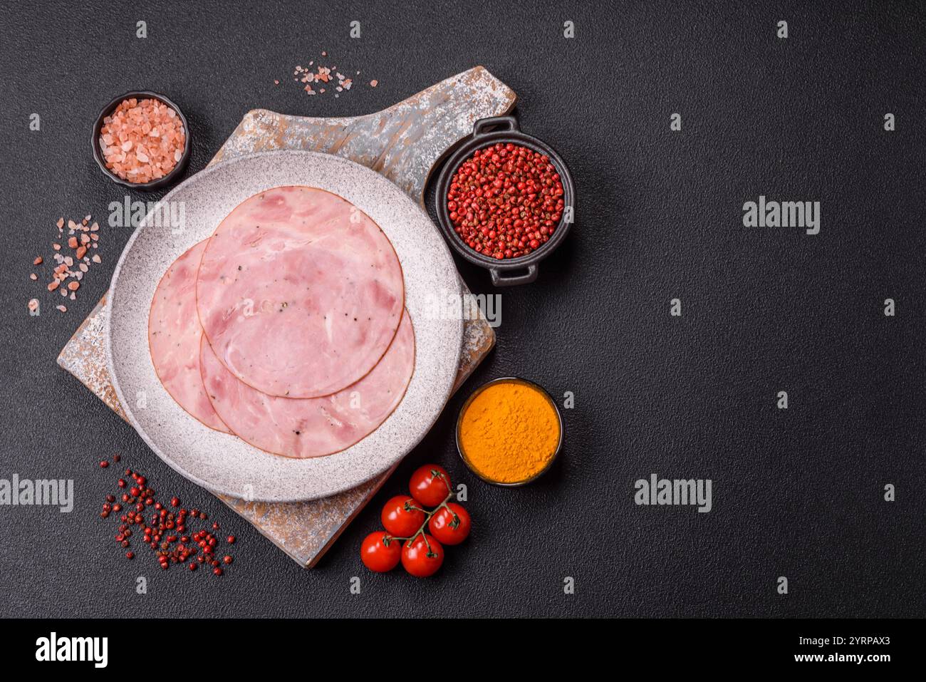 Smoked ham with salt, spices and herbs cut into round slices on a dark ...