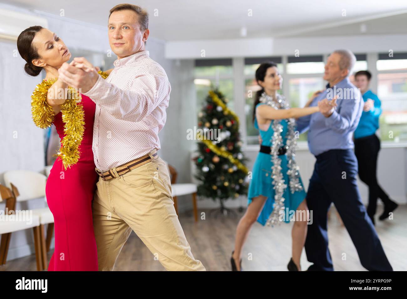 Couples dancing during Christmas - men and women dancing tango or samba next to Christmas tree ...