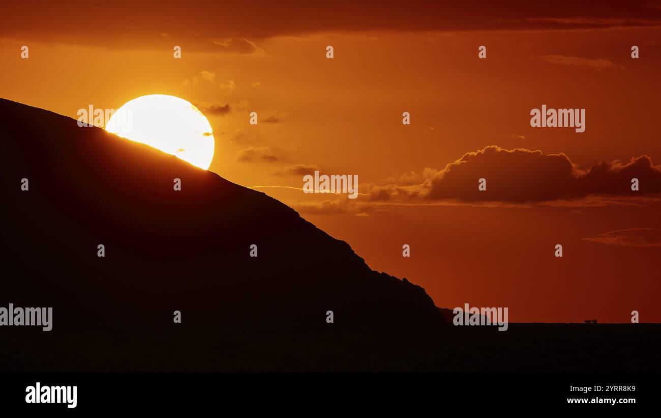 Sun disappears behind mountain, bright warm orange sky at sunset ...