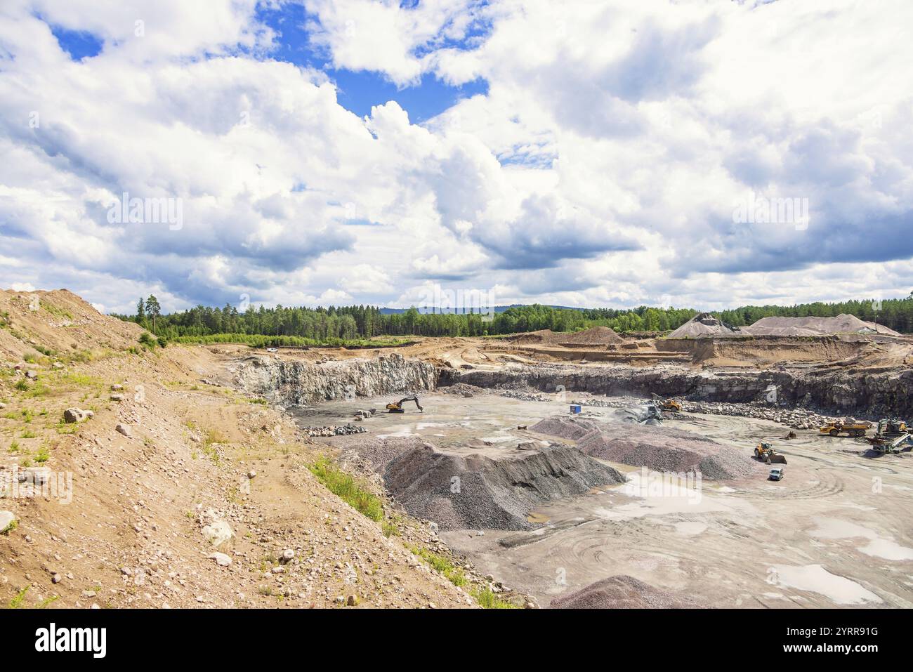 Active quarry with piles of gravel and machinery in a forest landscape ...