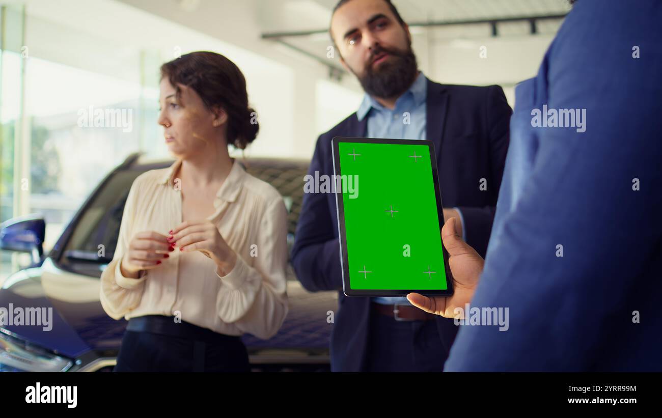Dealership salesman showing car models on green screen tablet to ...