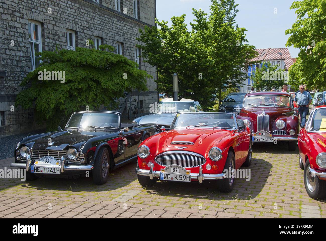 A row of classic convertibles stands on a paved square in the sun ...