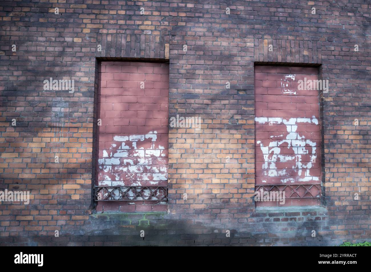 Weathered brick wall with two boarded up windows and peeling paint ...