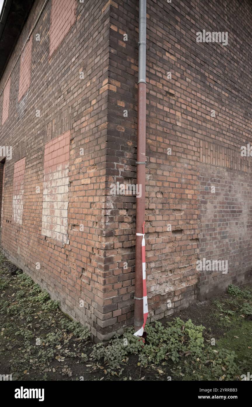 Red and white barrier tape wrapped around a downspout on an old brick ...