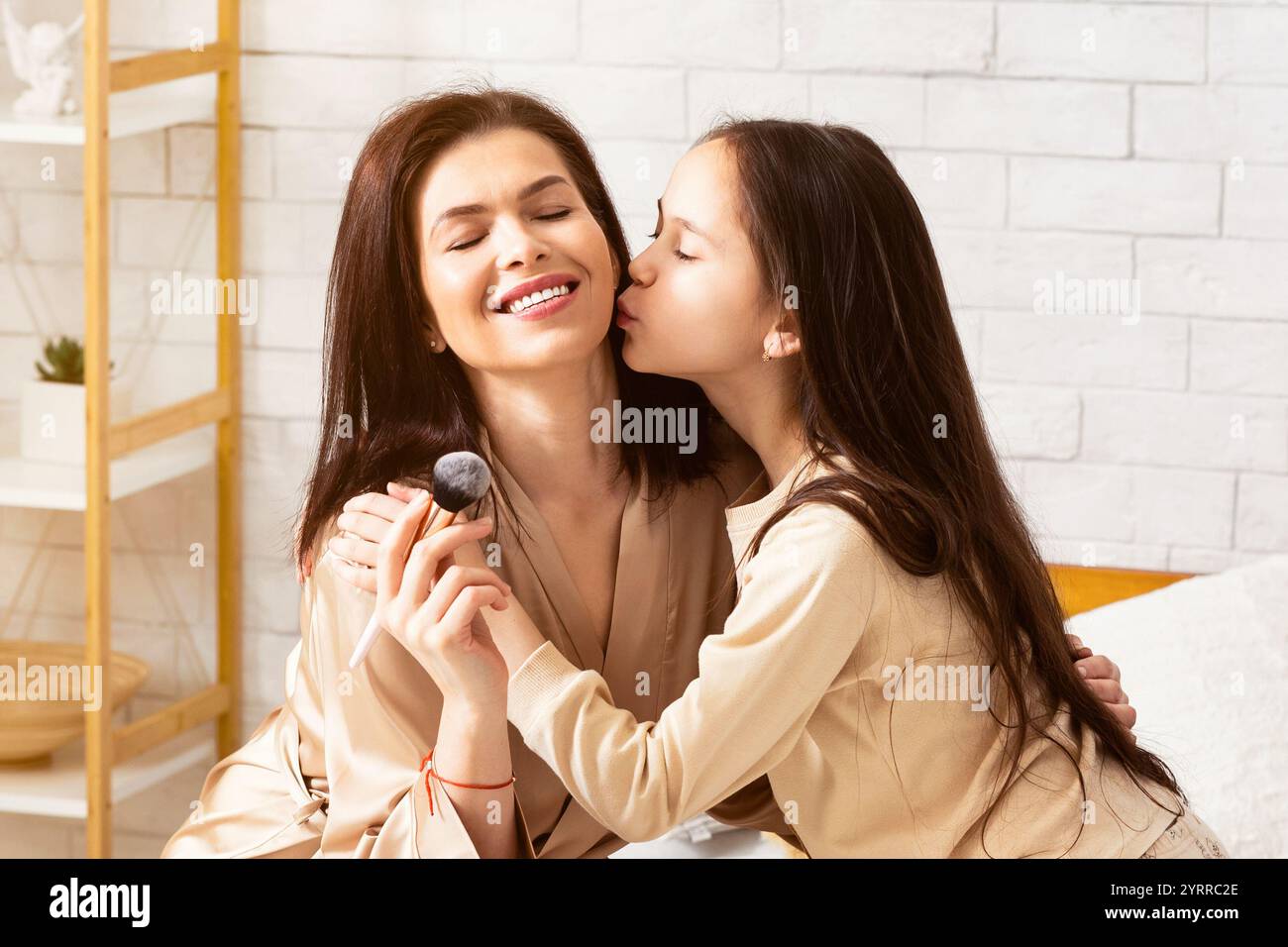 Makeup day at home. Teen girl kissing her mom on bed with scattered ...