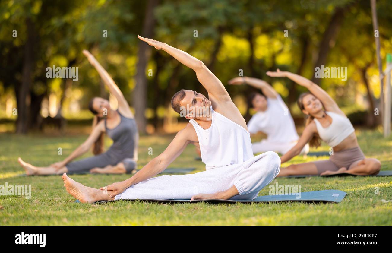 Man performing stretching yoga asanas during group session in park ...