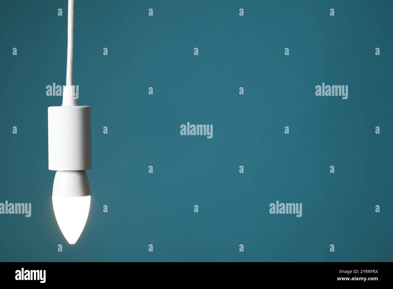 Light bulb hanging on cord against teal background, space for text ...