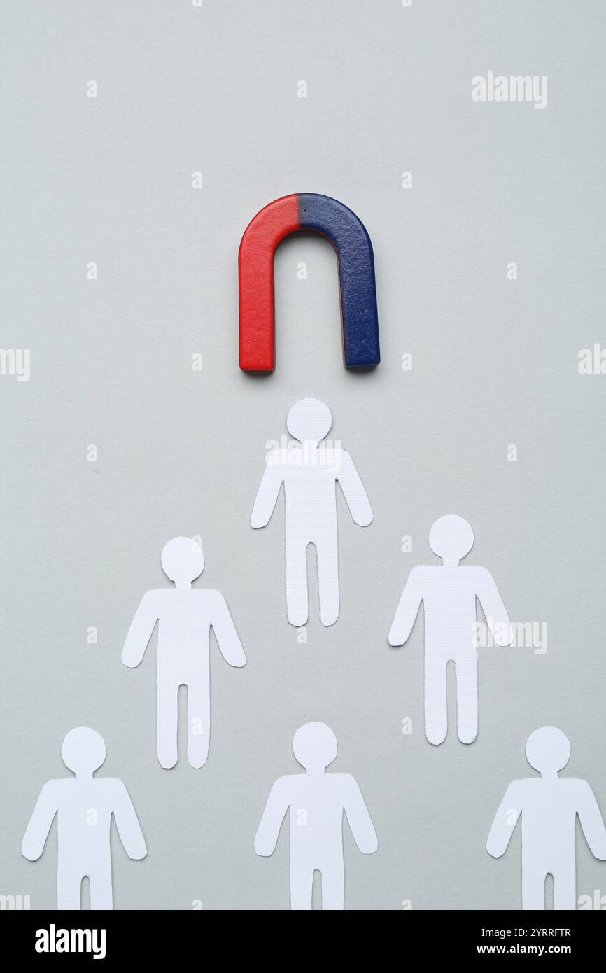Magnet attracting paper cutouts of humans on light grey background ...
