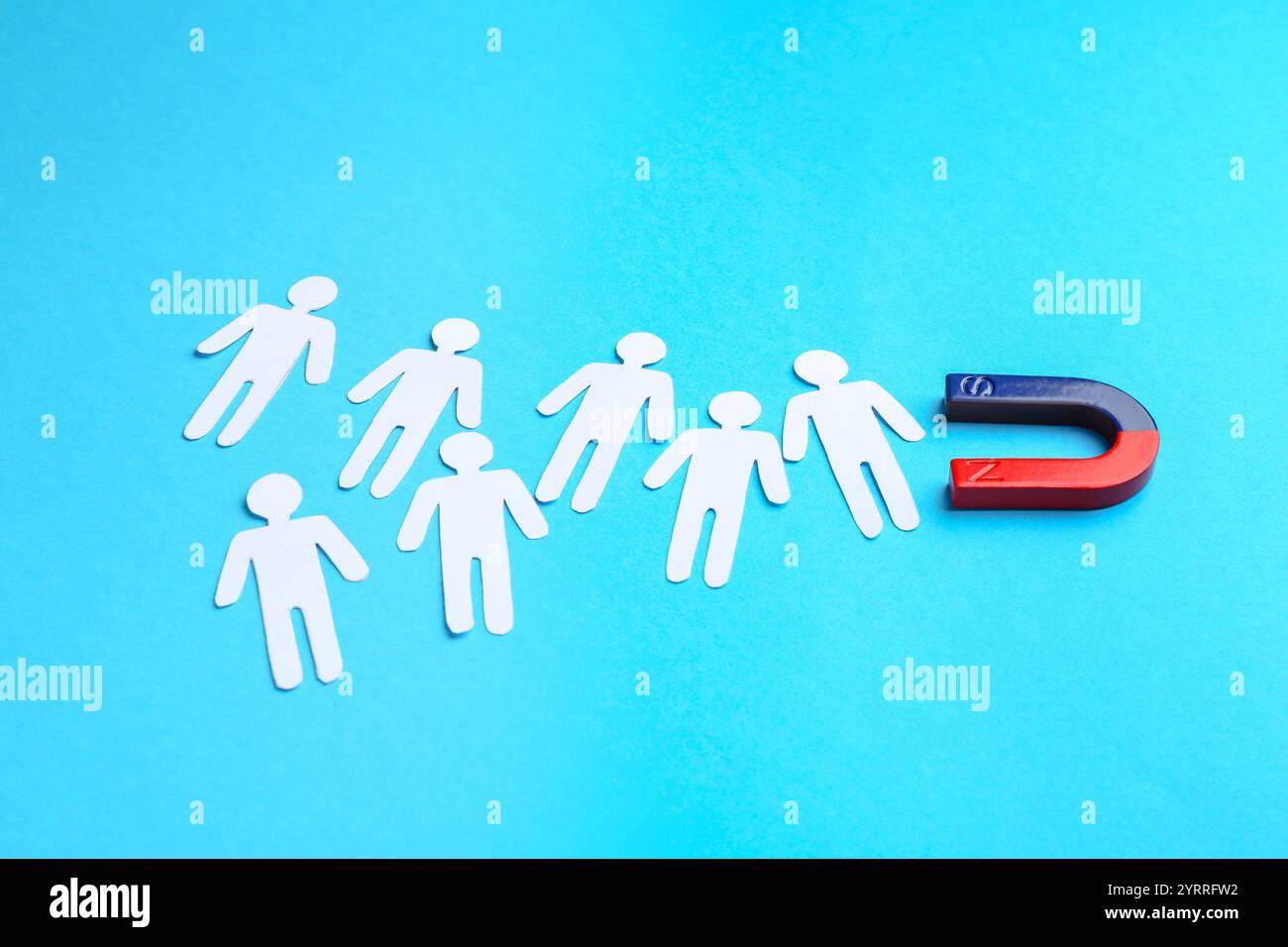 Magnet attracting paper cutouts of humans on light blue background ...