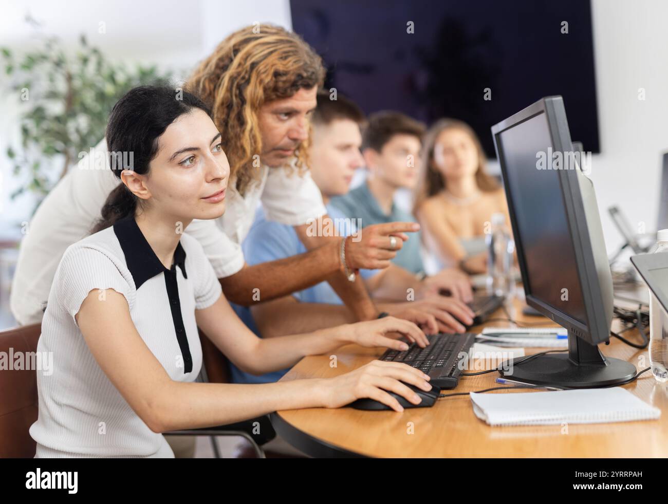 During computer lesson, male teacher helps girl student complete ...