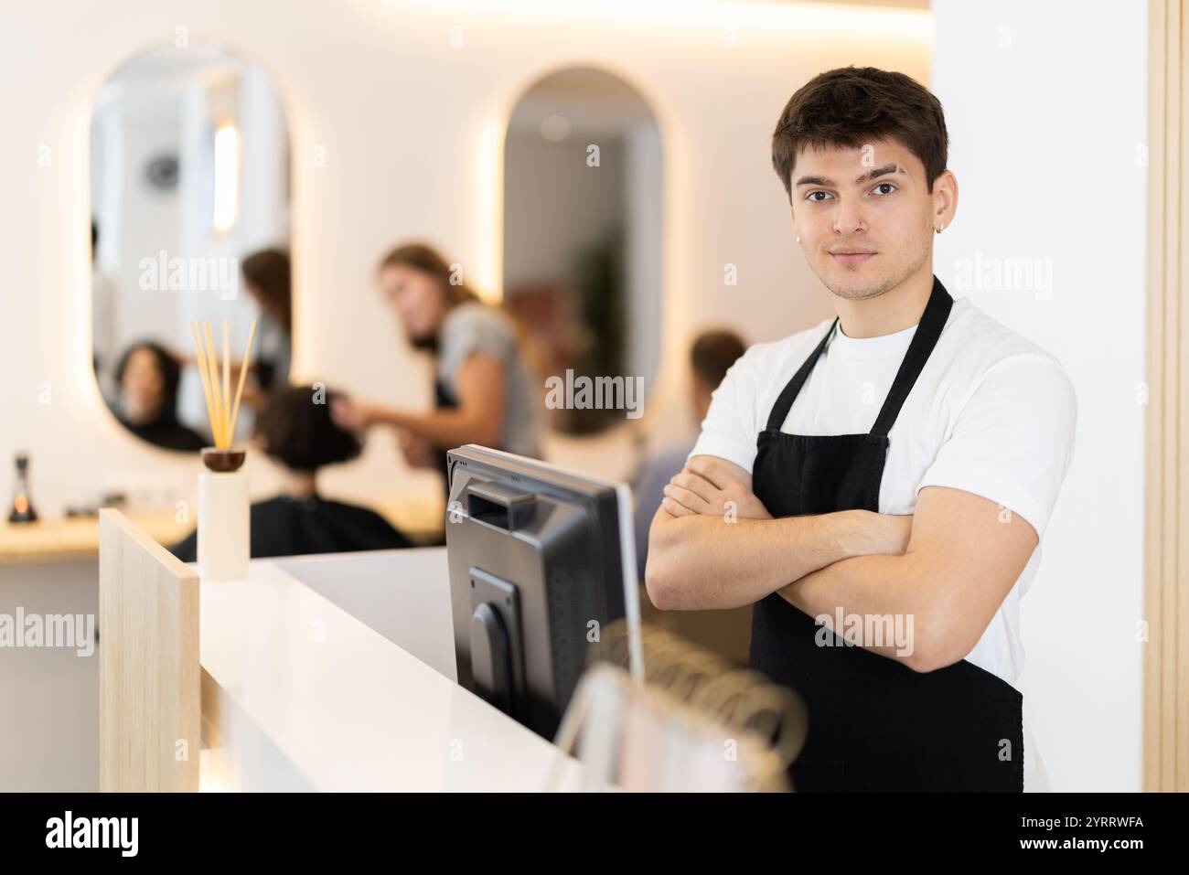 Male employee of barbershop stands near reception desk of salon, waits ...