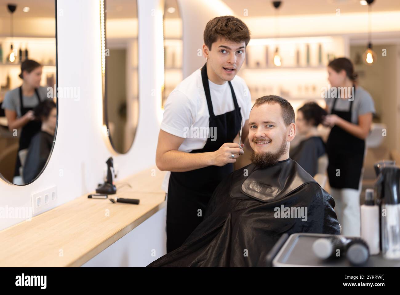 Young guy hairdresser giving haircut to young man Stock Photo - Alamy