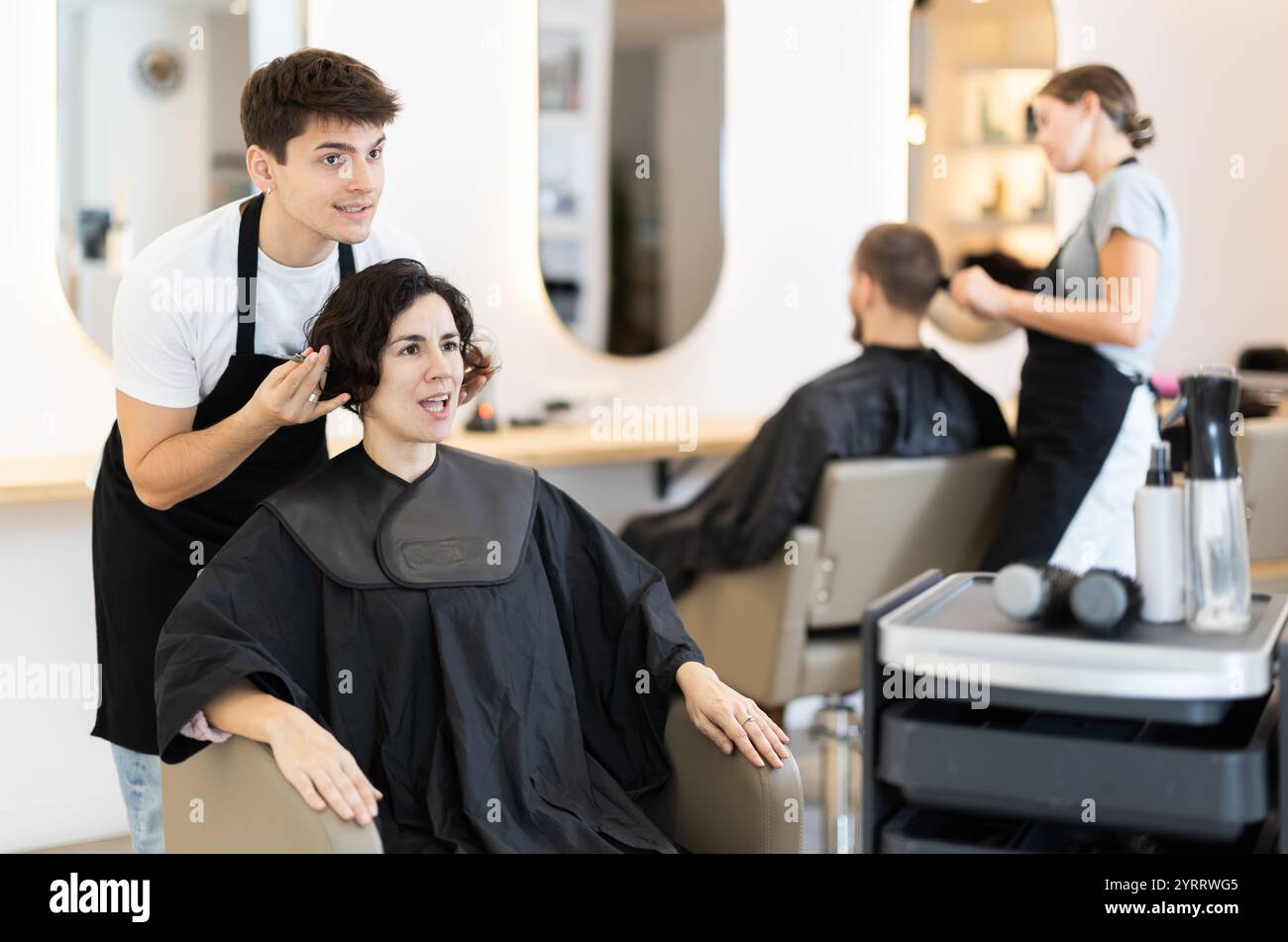 Young guy hairdresser giving haircut to adult woman Stock Photo - Alamy
