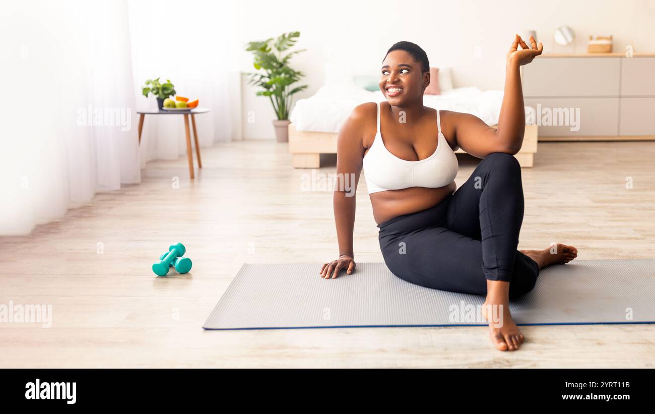 Plus size black woman resting on yoga mat after domestic training ...