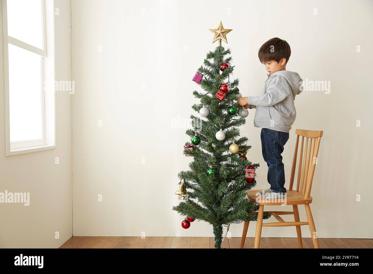 A boy decorating a Christmas tree using a chair as a stand Stock Photo ...