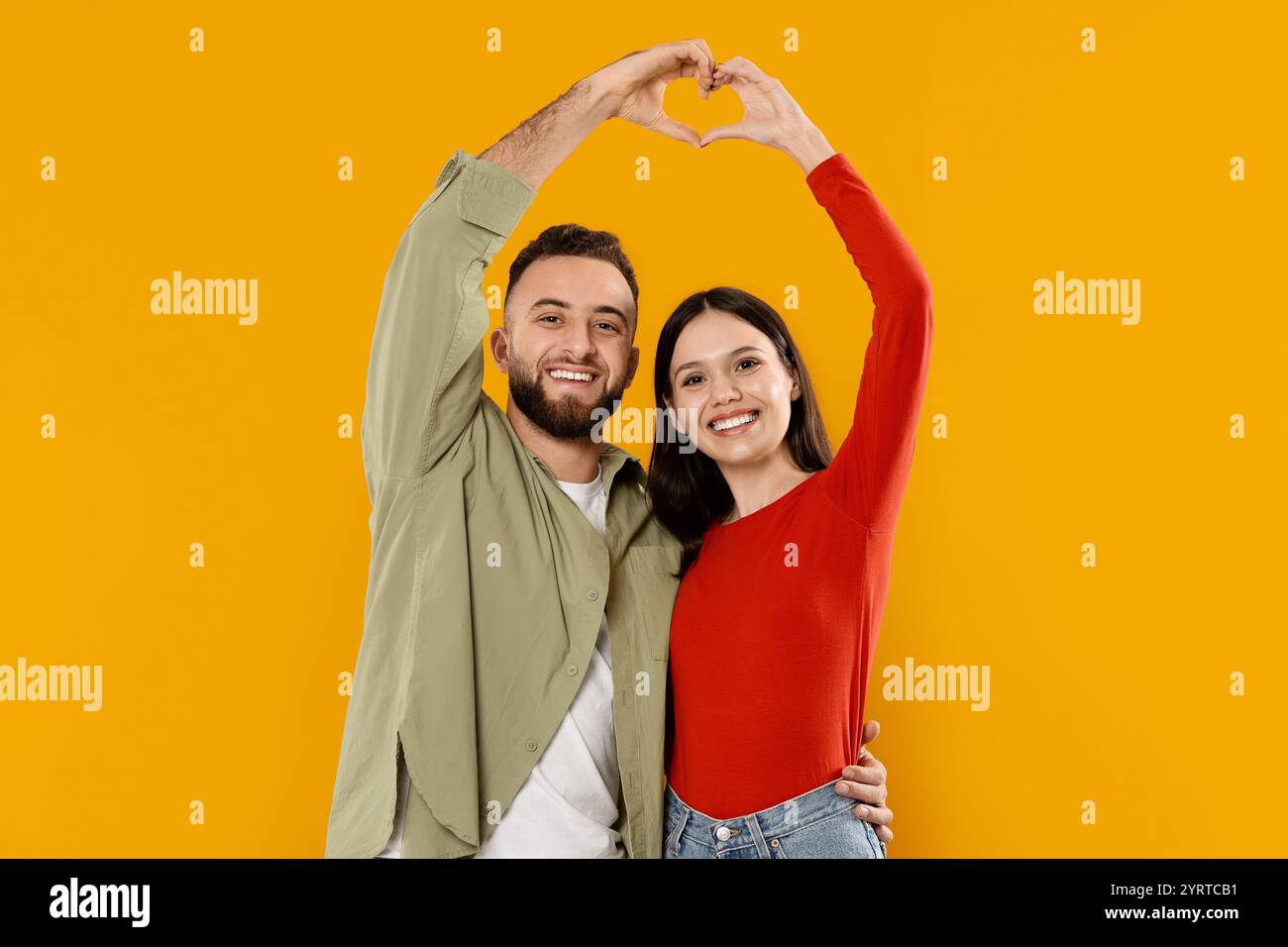Couple shares affection with heart gesture against vibrant yellow ...