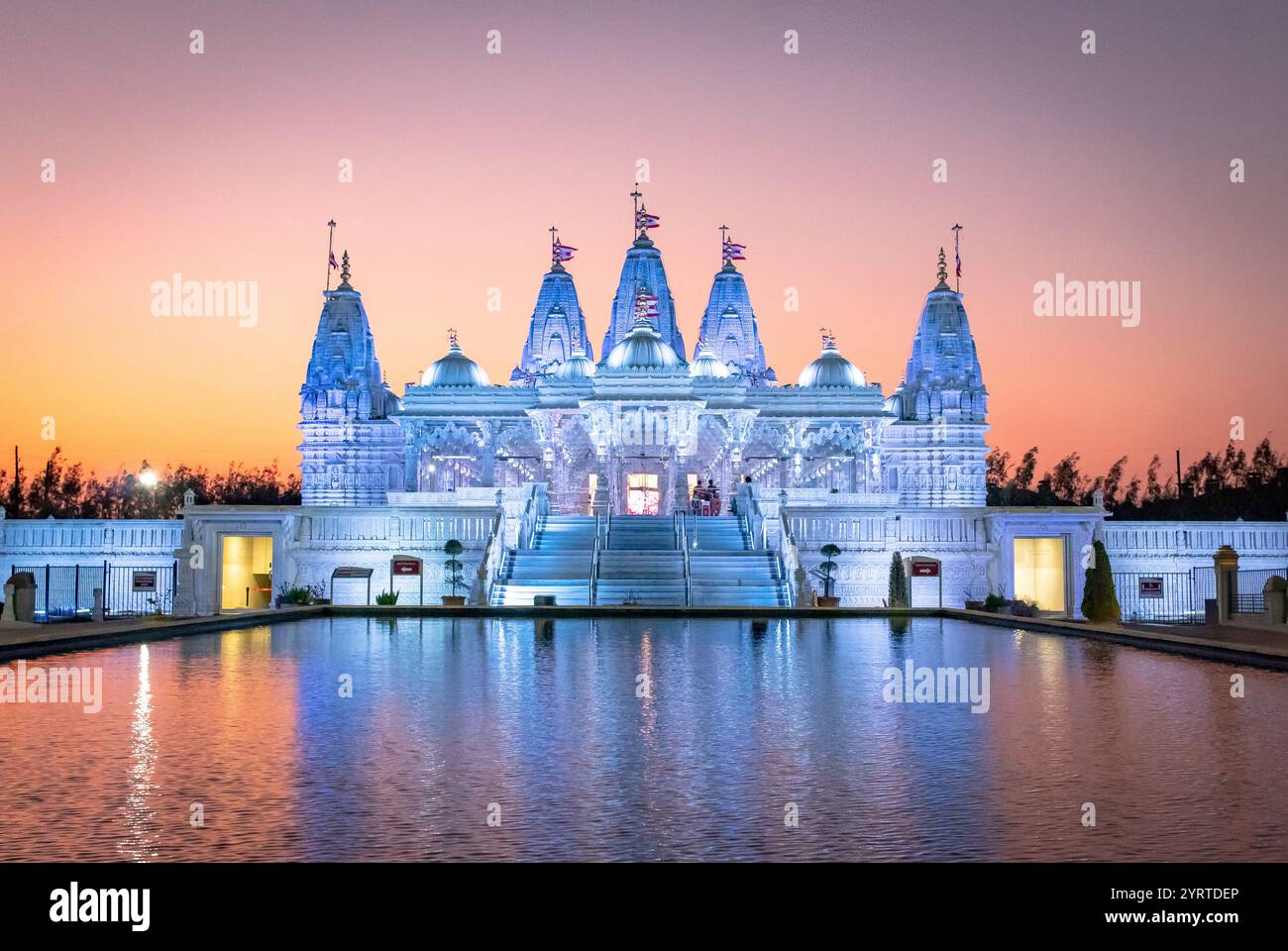 Blue illuminated BAPS Shri Swaminarayan Mandir reflected against water ...
