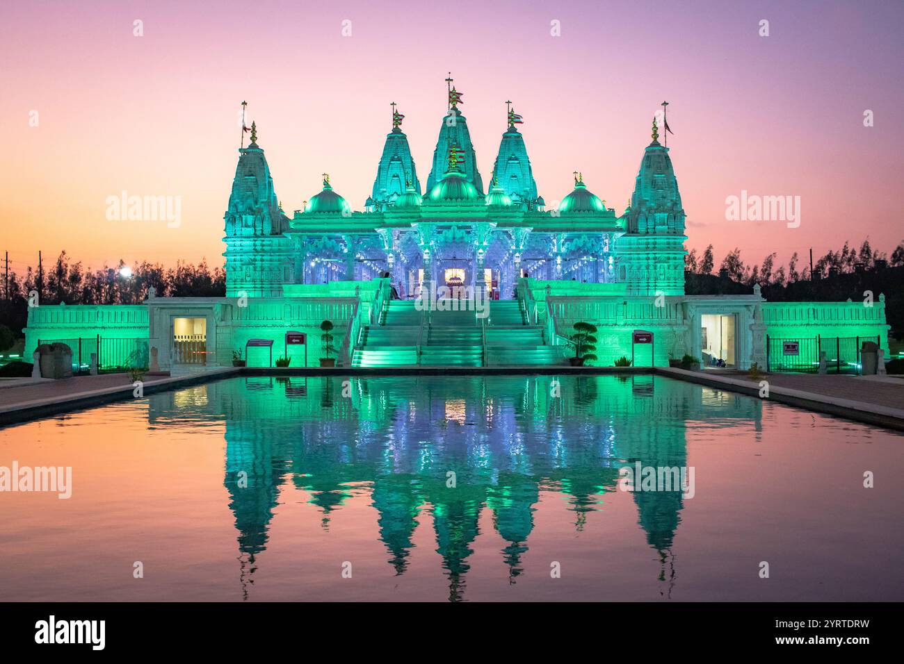 Green illuminated BAPS Shri Swaminarayan Mandir reflected against water ...