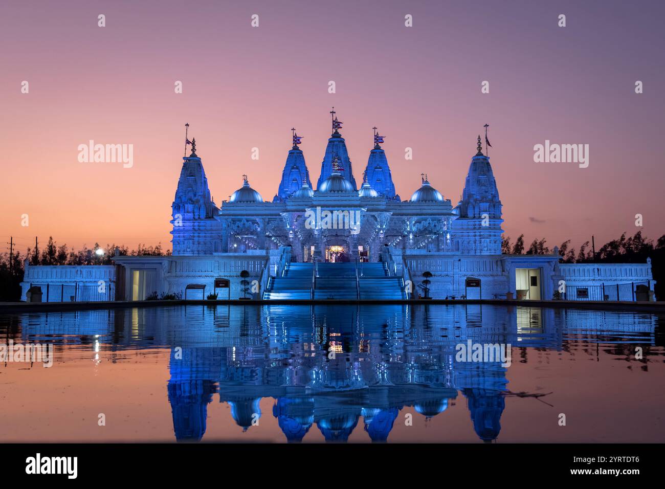 Blue illuminated BAPS Shri Swaminarayan Mandir reflected against water ...