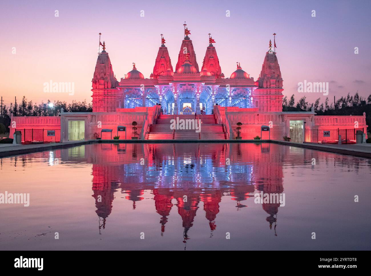 Red illuminated BAPS Shri Swaminarayan Mandir reflected against water ...