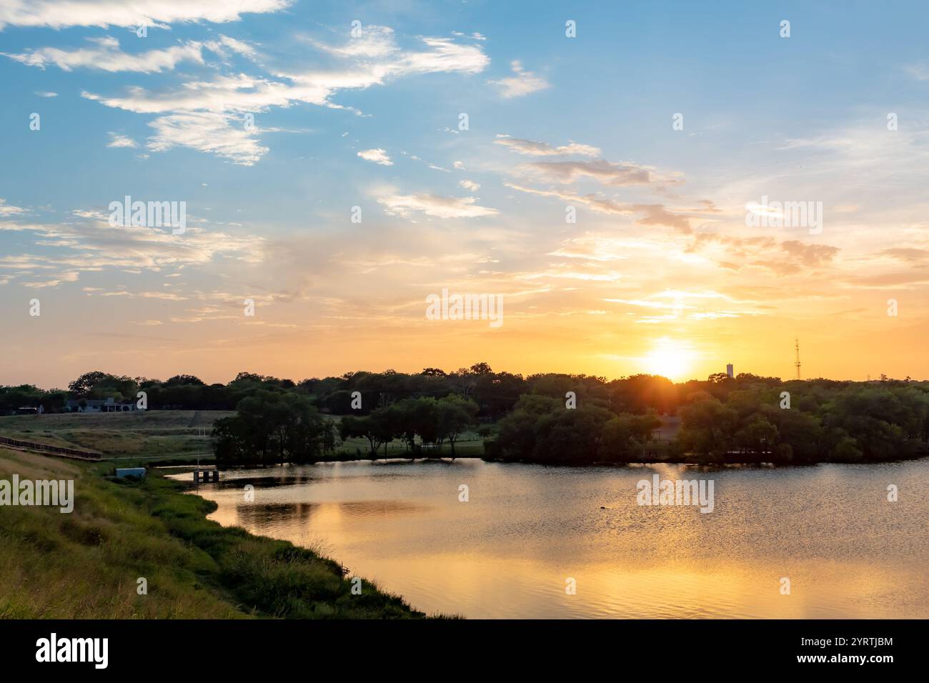 Dramatic golden sunset and clouds reflected along the treelined horizon ...