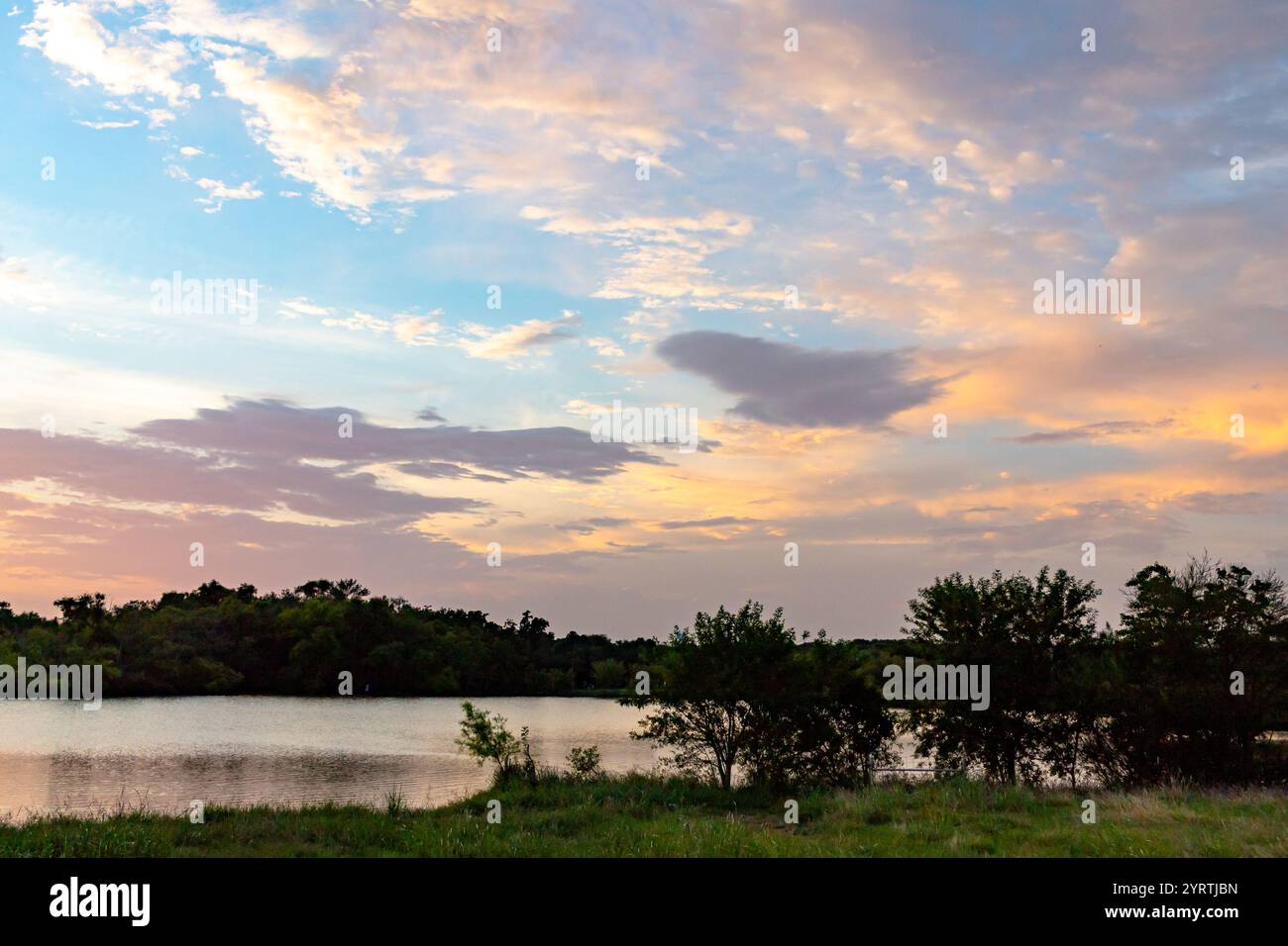 Dramatic golden sunset and clouds reflected along the treelined horizon ...