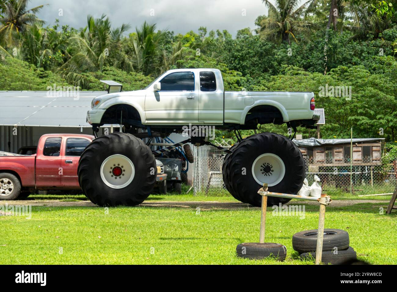 Modified truck on large tires parked beside a boat in a grassy area ...
