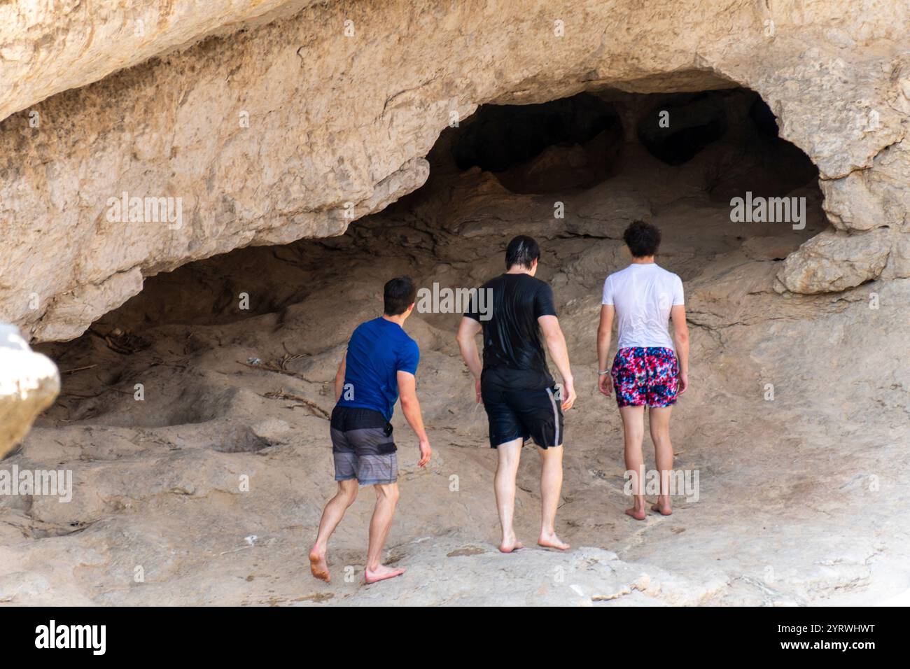 Group of friends exploring a rocky cave near the beach on a sunny day ...