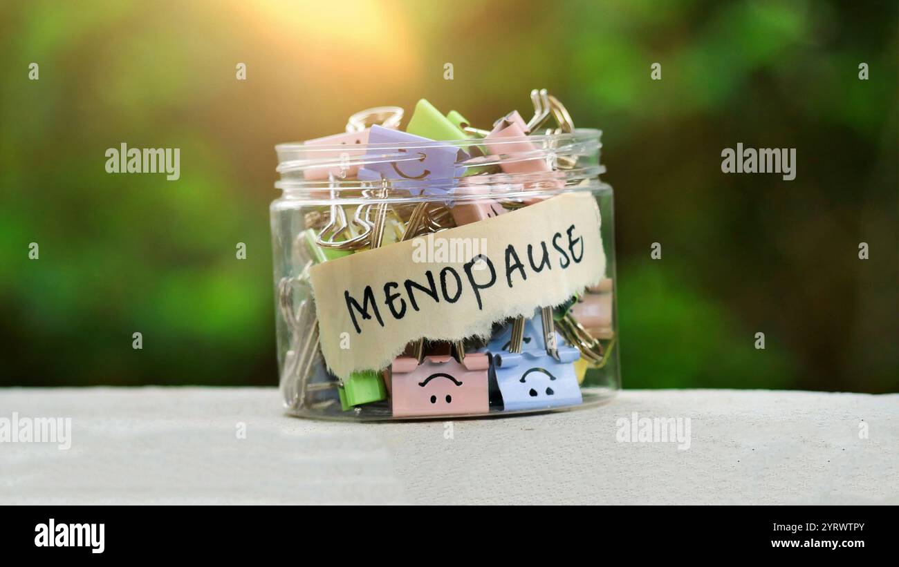 A clear jar contains paper clips of smiling and sad emojis on a blurred ...