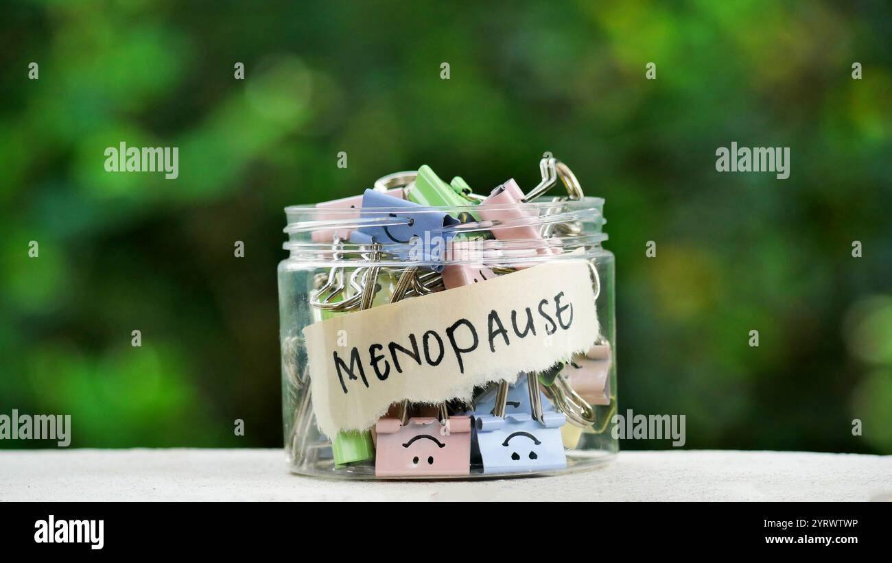 A clear jar contains paper clips of smiling and sad emojis on a blurred ...