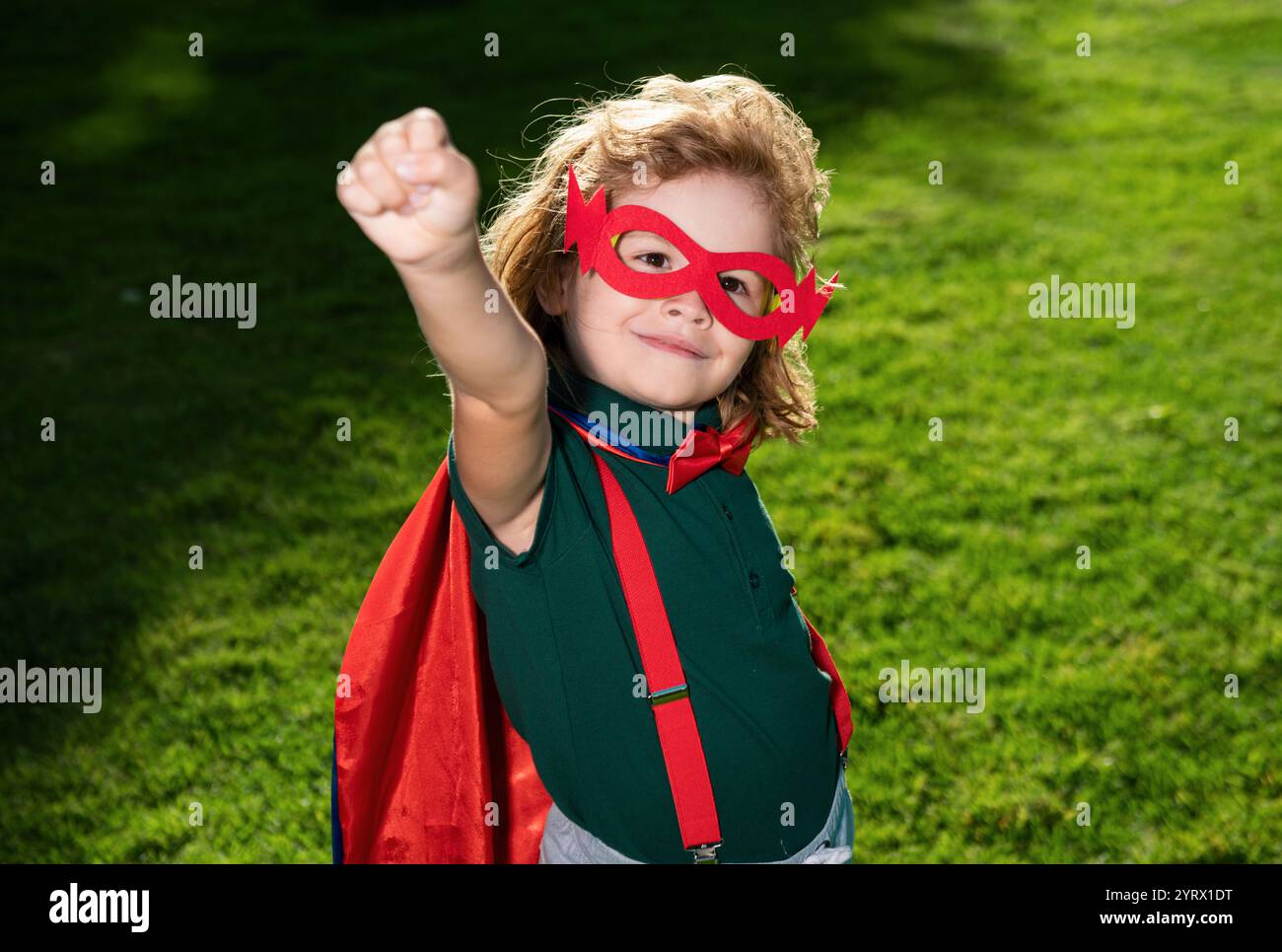 Brave boy in a superhero costume, wearing a red Cape and mask, held out ...