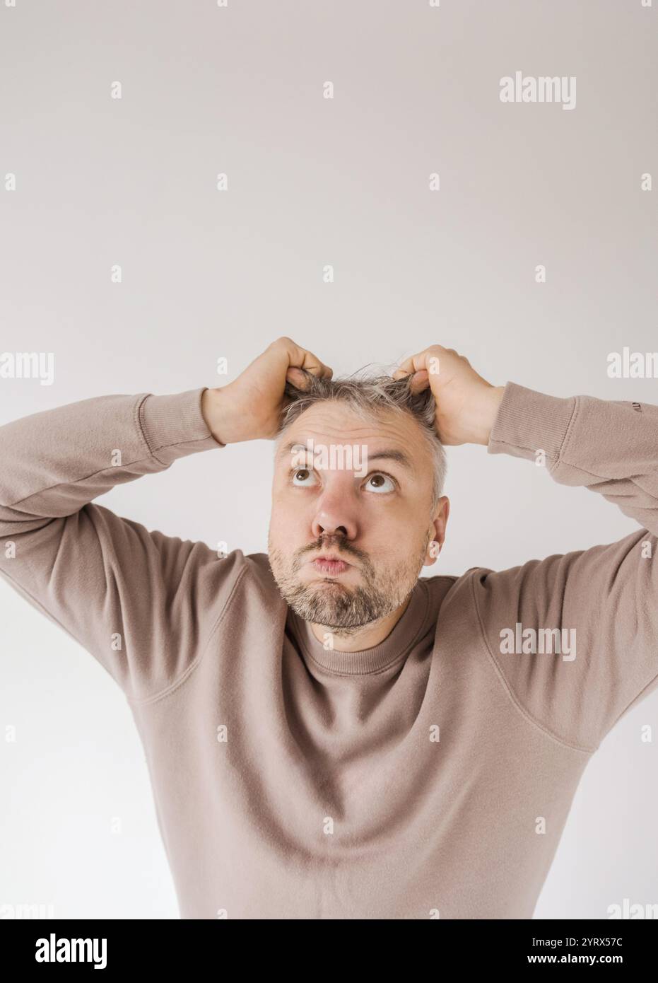 A portrait of a man with his hands in his hair, looking upward with a ...