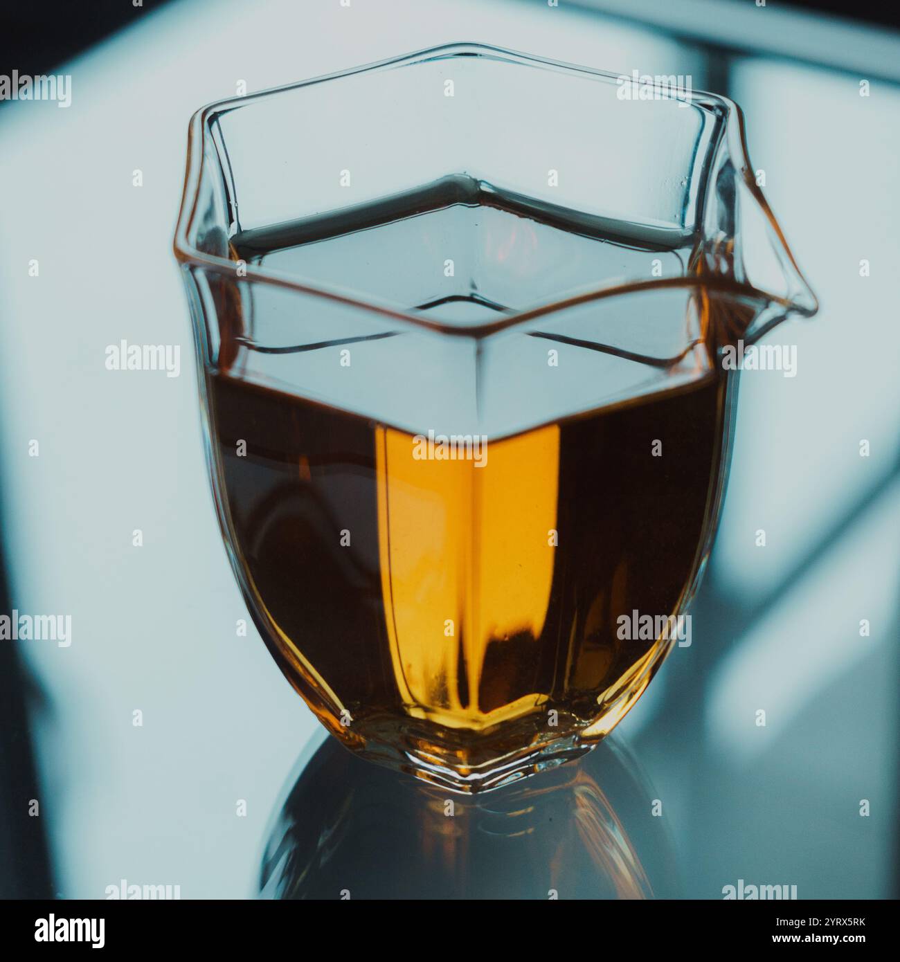 A stylish glass pitcher filled with vibrant amber liquid that stands ...