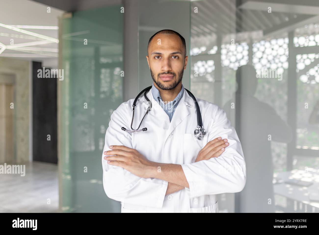 A confident doctor with arms crossed stands in a modern medical office ...