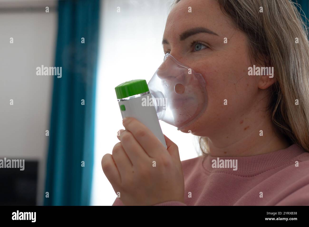 Young woman use a nebulizer for respiratory treatment. She holds the ...