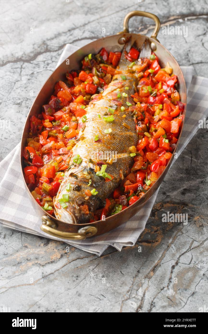Caribbean stew of whole sea fish with vegetables close-up in a frying ...