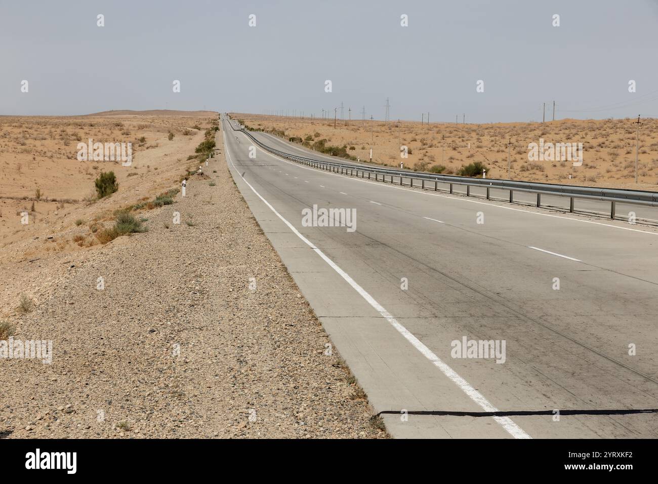 A wide concrete road extends through the barren desert of Uzbekistan ...