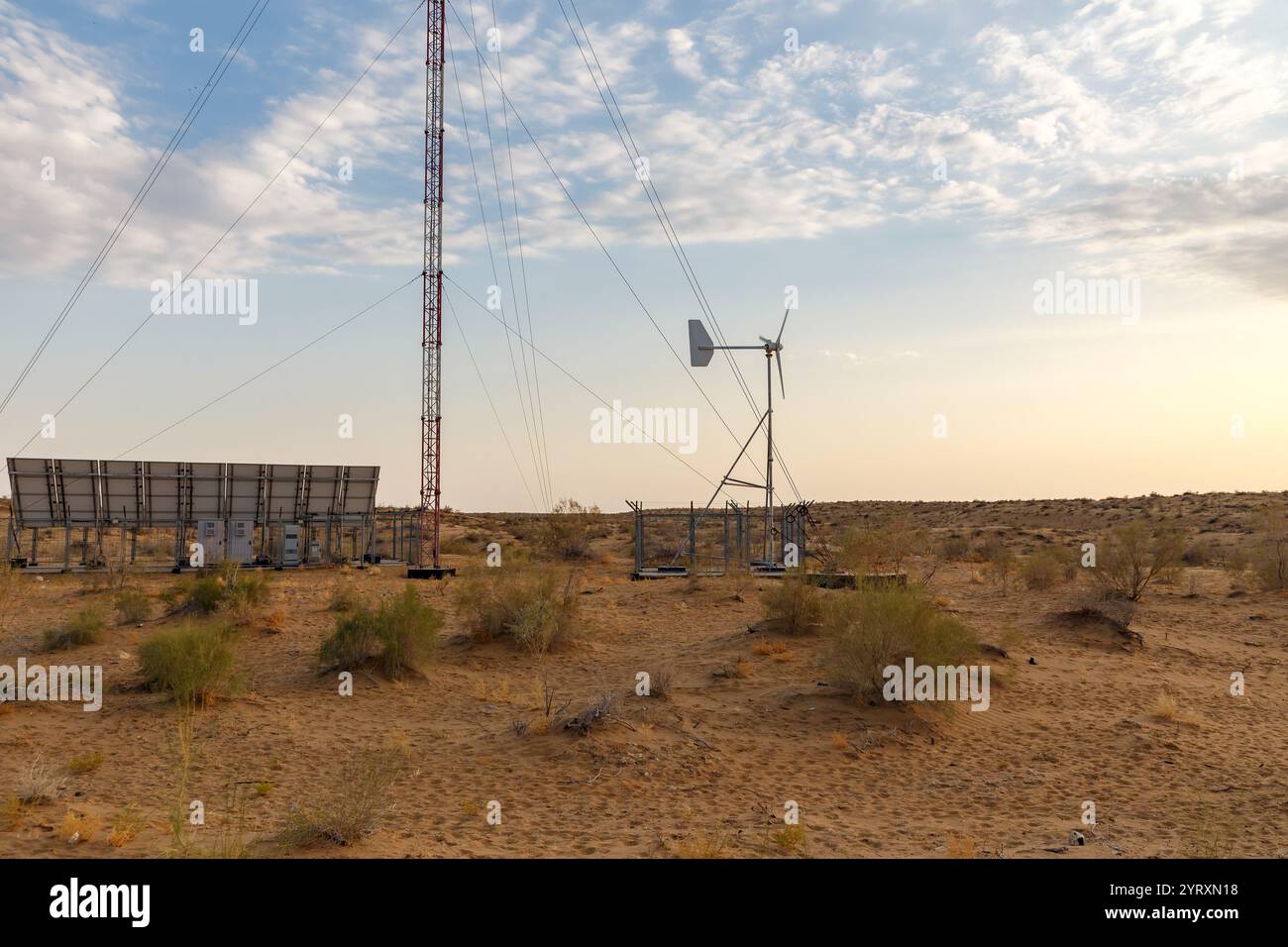 A cell tower stands alongside solar panels and a wind turbine ...
